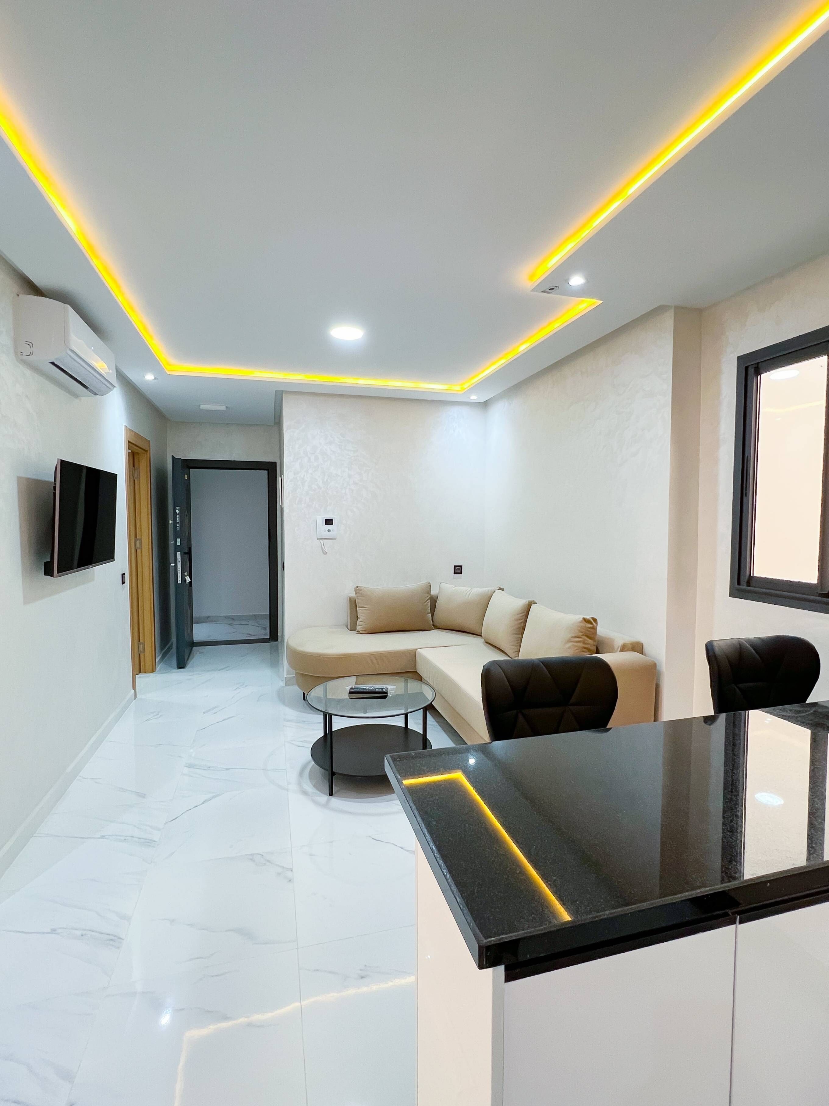 Uma sala de estar moderna com um sofá modular, uma mesa de centro de vidro e uma mesa de jantar preta com iluminação LED amarela.