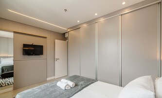 Quarto moderno com cama, televisão de tela plana na parede e guarda-roupa com portas de correr.