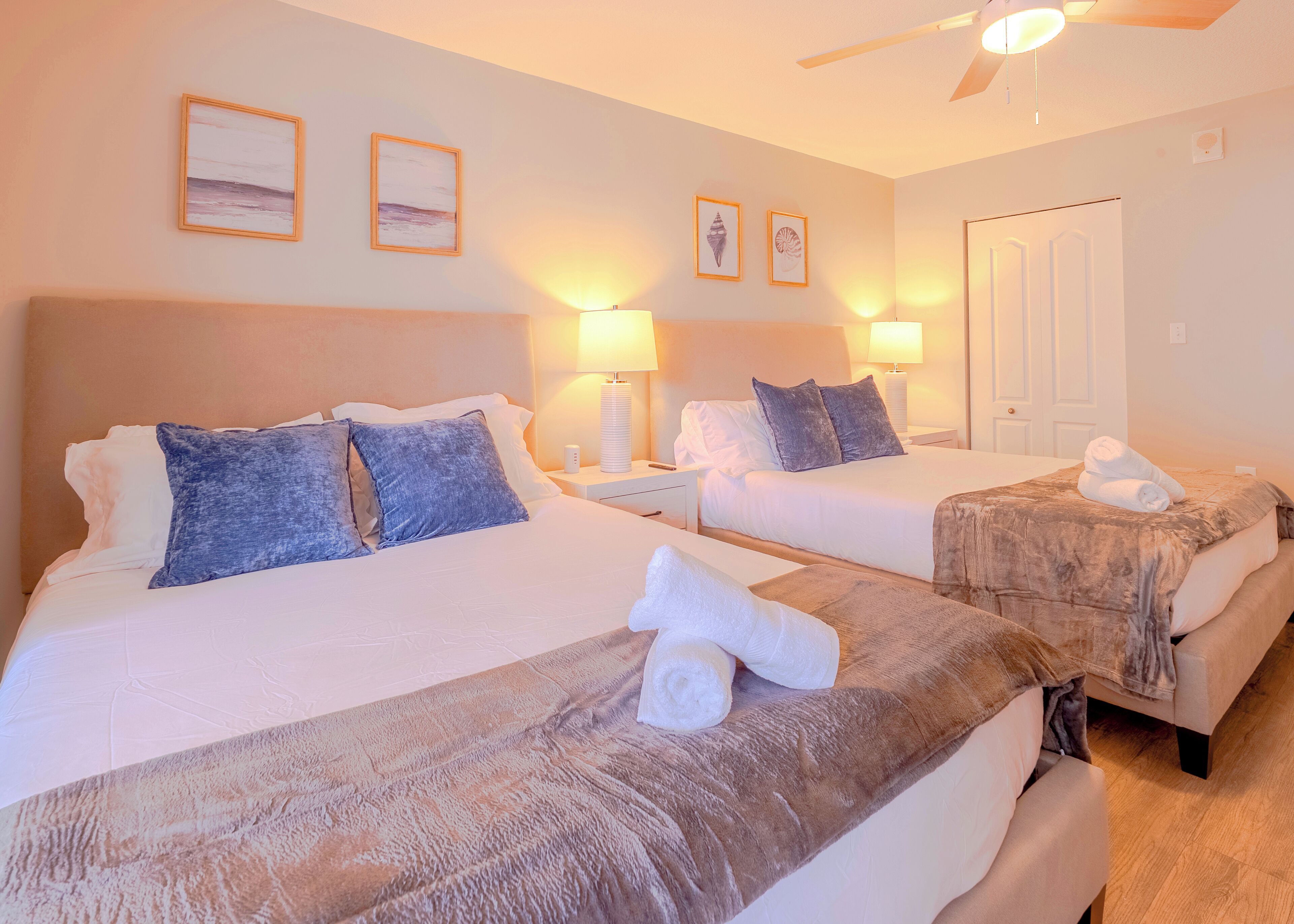 Quarto de hotel com duas camas, cada uma com cabeceira, mesas de cabeceira, luminárias e toalhas.