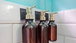 Três garrafas castanhas com bombas fixadas numa parede de azulejos brancos.