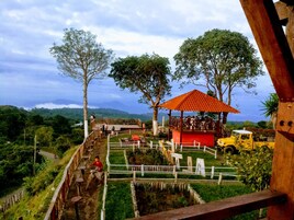 Um deck de madeira com um pavilhão de telhado vermelho, cercado por vegetação exuberante e um cenário montanhoso.