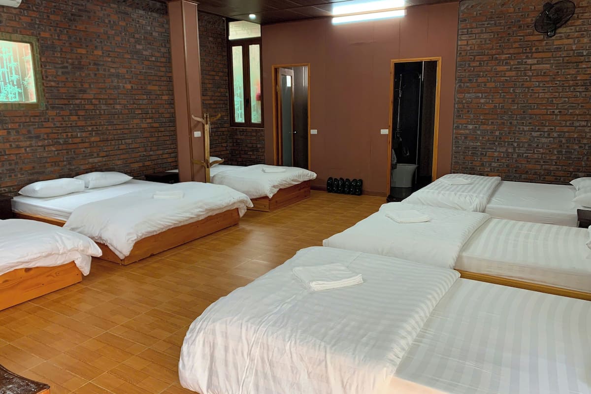 Quarto de hotel com várias camas, piso de madeira, paredes de tijolo e um espelho grande.