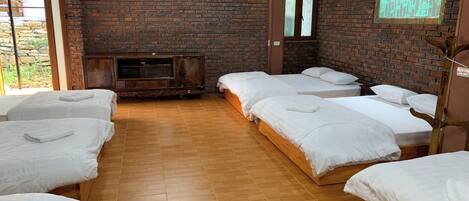 Quarto de hotel com quatro camas, parede de tijolos, piso de madeira e uma televisão.