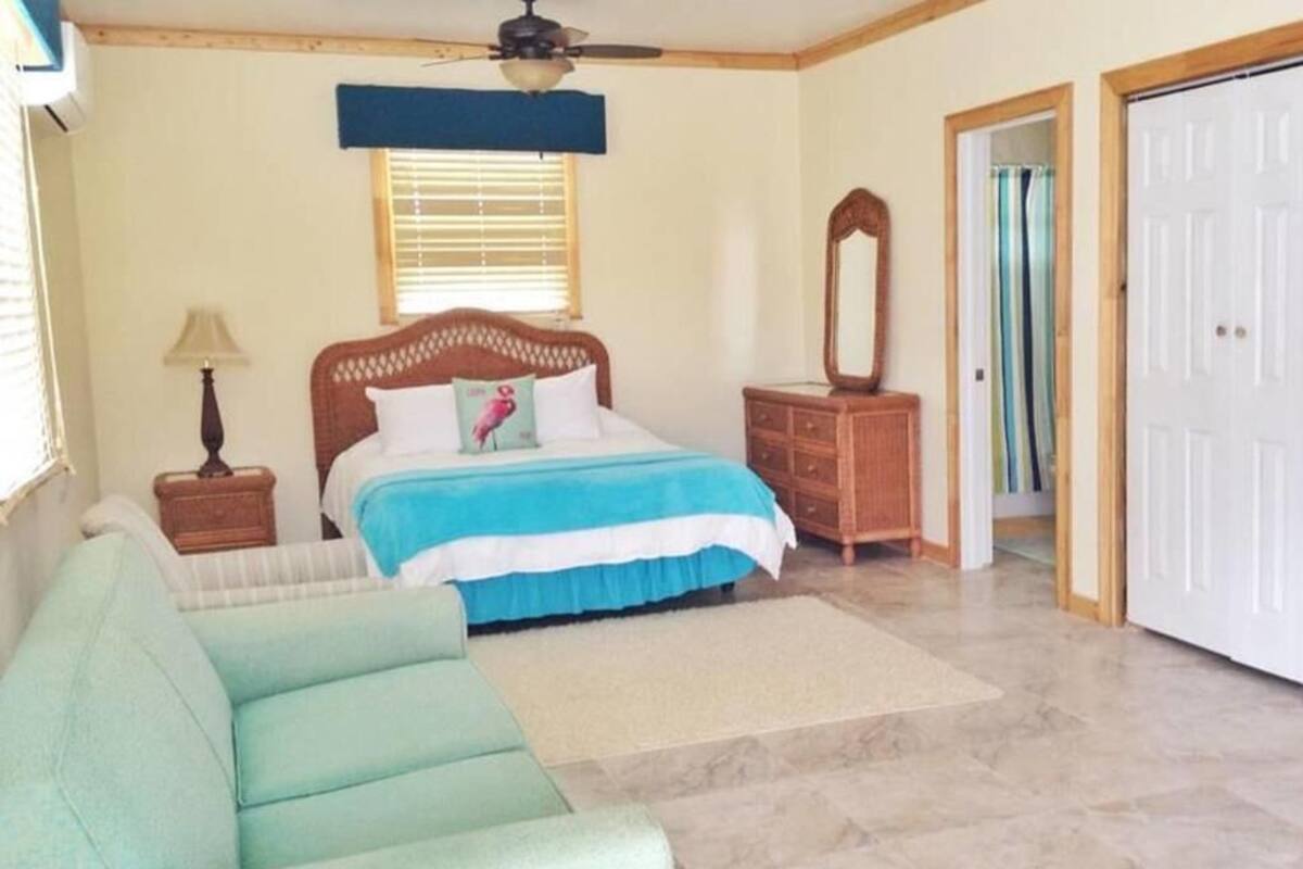 Um quarto com cama, mesa de cabeceira, cômoda, espelho e porta.
