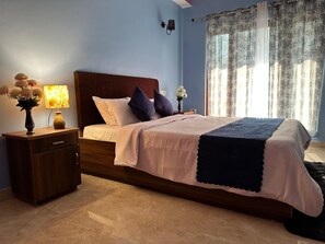 Quarto com cama de madeira, mesa de cabeceira com abajur e um vaso de flores.