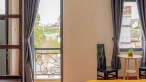 Quarto de hotel com uma cama, uma mesinha com uma planta, uma cadeira e varanda com guarda-corpo.