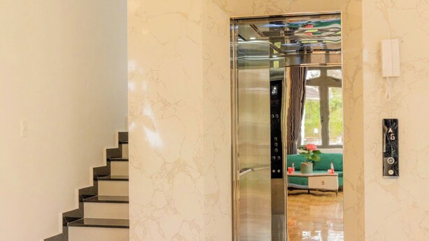 Um interior moderno com uma parede de mármore, um elevador de vidro e uma escadaria.