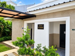 Entrada de um edifício com uma placa indicando 'MASJID AT TAQWA' e uma área externa coberta com plantas.