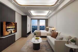 Quarto de hotel moderno com um piano, uma cama grande, um sofá, uma mesa de centro e vista para a cidade.