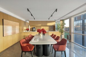 Uma sala de conferências moderna com uma mesa comprida, cadeiras vermelhas e uma grande janela com vista para a cidade.