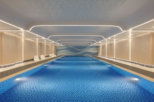 Uma piscina interior comprida e estreita, com chão e paredes azulejadas em azul, rodeada por painéis de madeira e iluminação embutida.