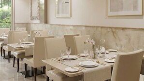 Uma sala de jantar com mesas preparadas para o serviço, piso de mármore e quadros nas paredes.