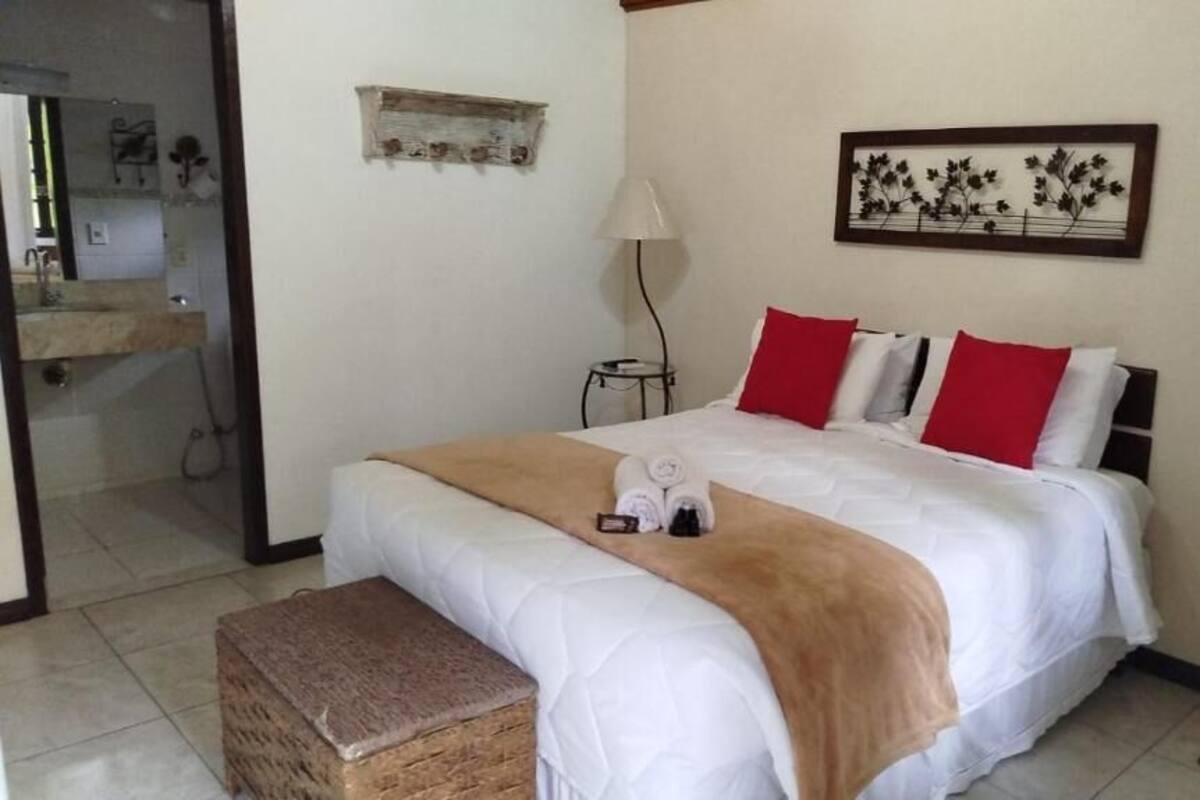 Quarto bem arrumado com cama, mesa de cabeceira, abajur e quadro na parede.