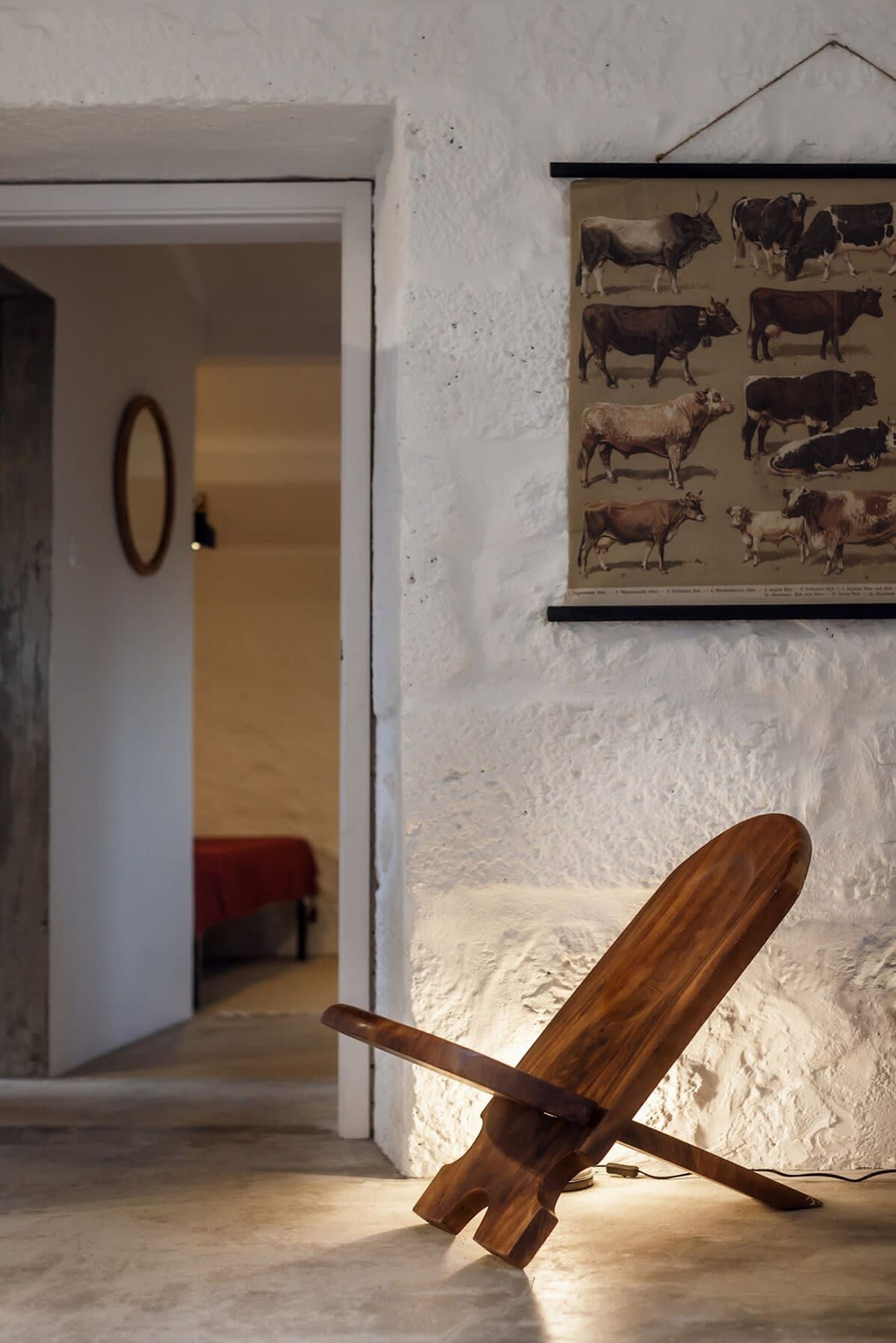 Quarto com uma escultura de madeira no chão, uma ilustração de animal emoldurada na parede e uma porta de entrada para outro cômodo.