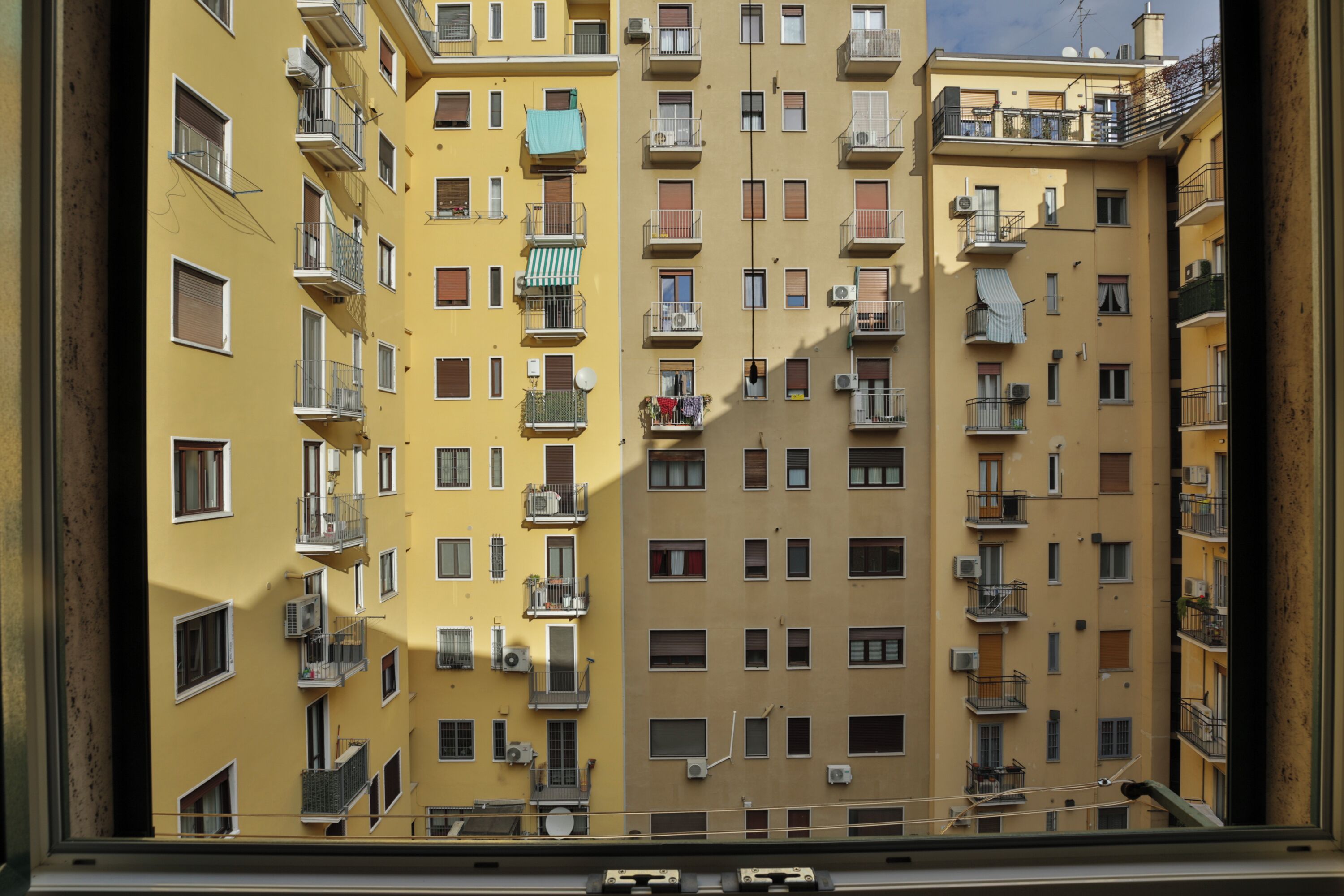 Um edifício residencial com vários andares, varandas, aparelhos de ar condicionado e uma janela com vista para a fachada do prédio.