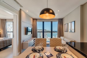Quarto de hotel moderno com área de refeições, cama, TV e vista da cidade.