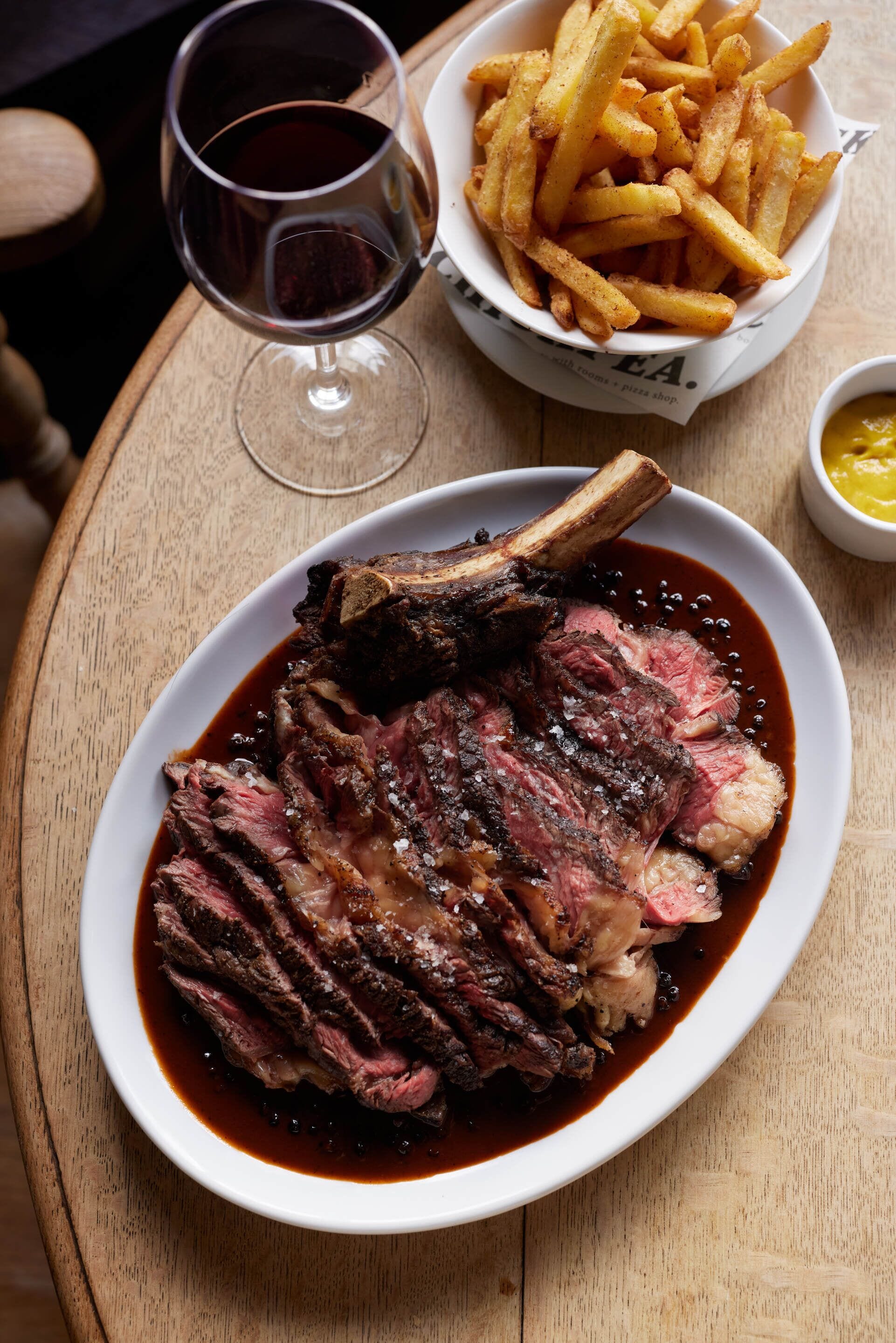 Um prato de bife com batatas fritas e um copo de vinho tinto sobre uma mesa de madeira.