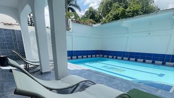 Uma área de piscina com espreguiçadeiras e piso revestido de azulejos.