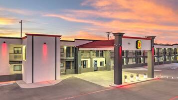 Entrada de hotel com telhado vermelho, vários andares e área de estacionamento.