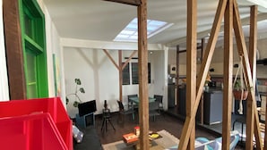 Uma área de estar ampla com teto alto, vigas de madeira, uma porta verde, um sofá, uma mesa de jantar e um espaço de cozinha.