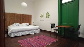 Quarto com uma cama, uma escrivaninha, duas cadeiras, uma porta verde e duas obras de arte na parede.