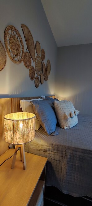 Quarto com cama, almofadas, abajur e decoração na parede.