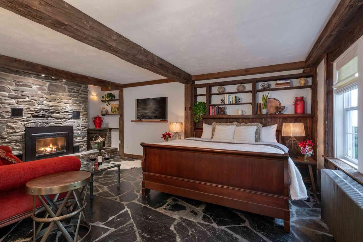 Quarto com lareira de pedra, cama grande, sofá vermelho e teto de madeira.