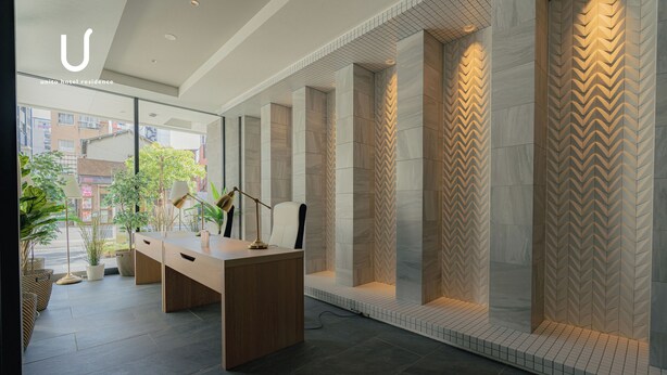 Uma área de recepção de hotel moderna, com uma mesa de madeira, uma luminária e um vaso de planta.