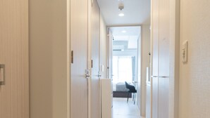 Um corredor de hotel moderno com design limpo e minimalista, apresentando paredes em tons claros, piso de madeira e uma cama ao fundo.