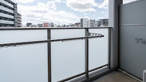 Uma varanda com grade de metal, vista para o horizonte urbano e um muro com texto em japonês.