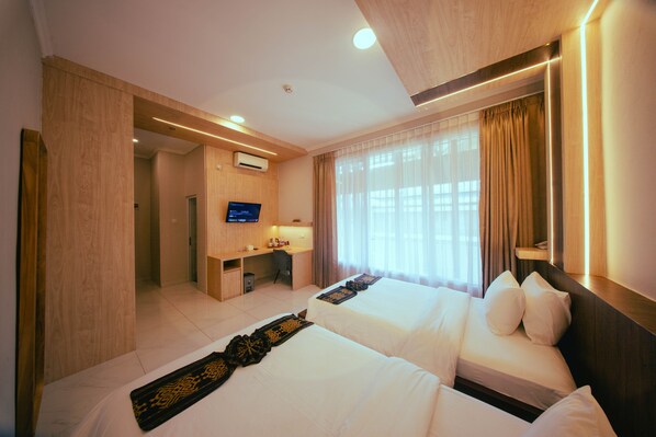 Quarto de hotel com duas camas, uma escrivaninha, televisão e uma janela grande com cortinas.