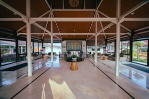 Um hall amplo com teto alto, janelas grandes e área de estar central com uma mesa de centro.