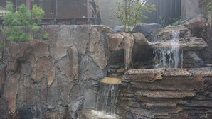 Jardim de pedras com uma pequena cascata e um lago.