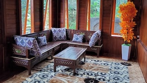 Interior de madeira com sofá, mesa de centro e uma janela grande com vista para o verde.
