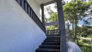 Uma escadaria com degraus pretos e parede branca, que leva a uma área coberta com corrimão.