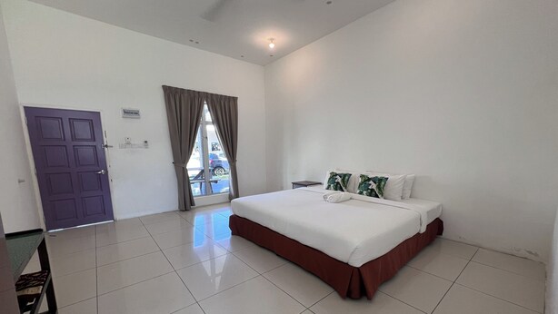 Quarto de hotel com uma cama grande, uma mesinha, uma porta roxa e vista para o exterior através de uma janela.