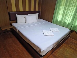 Cama bem arrumada com lençóis e almofadas brancos, cabeceira de madeira e cortina verde.