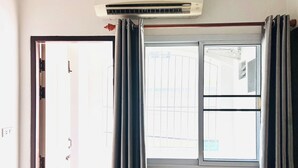Quarto com porta de vidro deslizante, janela com cortinas e ar condicionado acima da janela.
