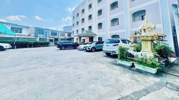 Hotel de vários andares com estacionamento, vários carros estacionados e um santuário decorativo.