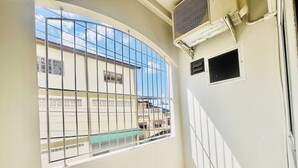 Quarto com uma janela grande, um ar condicionado pequeno e piso de azulejos.
