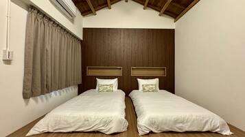 Quarto com duas camas, cabeceiras de madeira, teto com vigas de madeira e janela com cortinas.