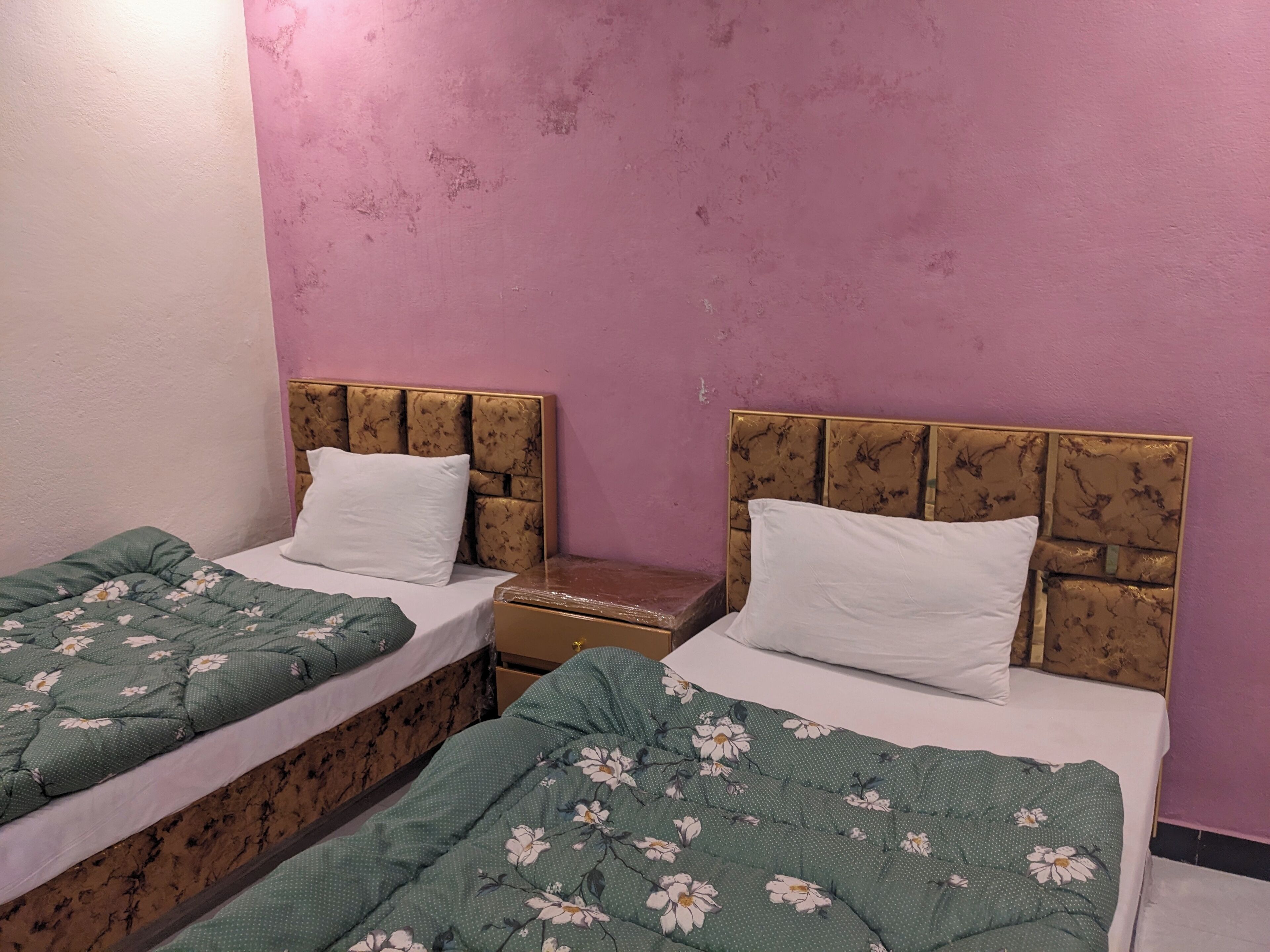 Quarto com duas camas, cada uma com roupa de cama estampada com motivos florais e cabeceiras de madeira.