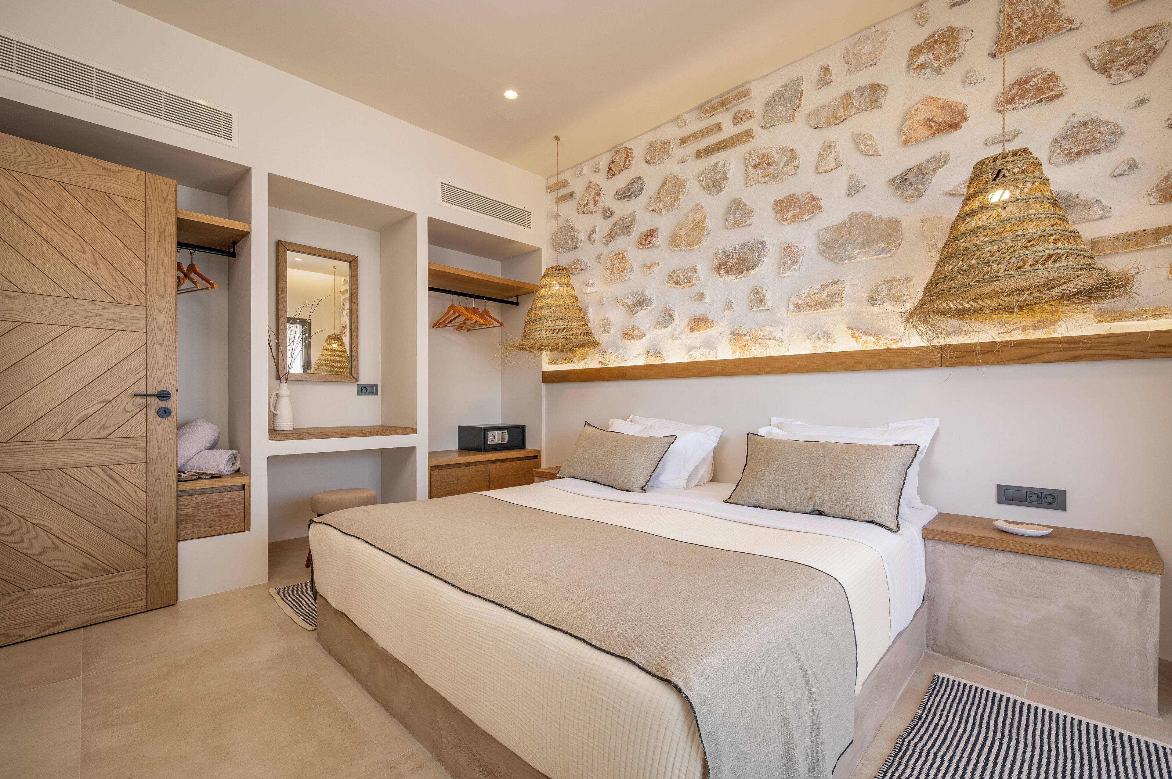 Quarto com cama grande, guarda-roupa de madeira, estantes embutidas, parede de pedra e luminária pendente.