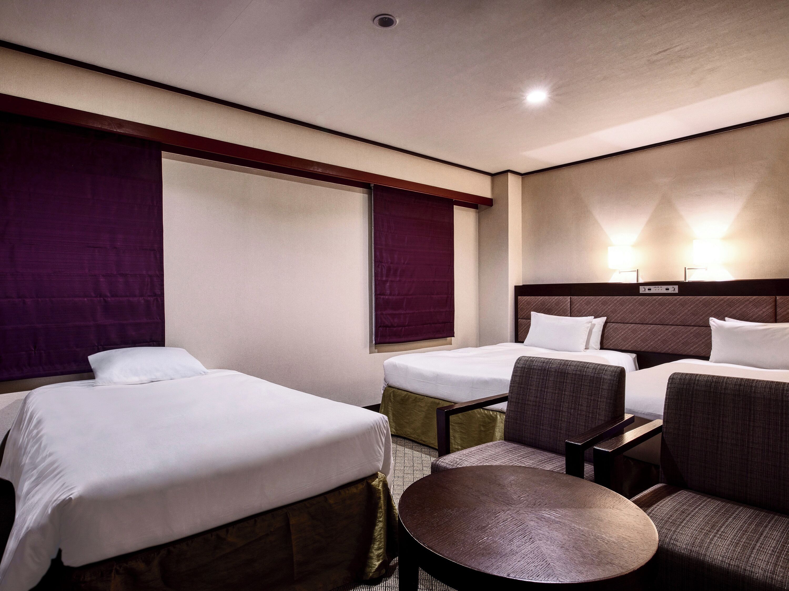 Quarto de hotel com duas camas, uma mesa redonda pequena e uma cadeira.