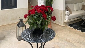 Quarto com mesa de mármore, planta em vaso com flores vermelhas, sofá e um candeeiro pendente.