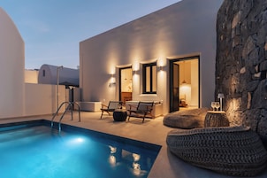 Uma área moderna de piscina ao ar livre com uma parede de pedra, duas cadeiras de descanso e uma mesa pequena com copos.