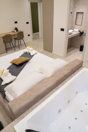Quarto de hotel moderno com uma cama grande, uma banheira separada, uma escrivaninha com cadeiras e um banheiro pequeno.