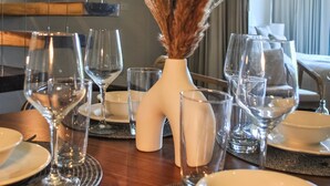 Uma mesa de jantar posta com copos transparentes, pratos e um vaso decorativo com plumas de capim-do-campo.