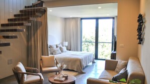 Quarto de hotel moderno com escada, cama com vista, sofá e mesa de centro.