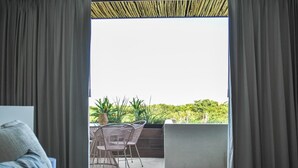 Quarto com cama e vista para um pátio externo com cadeiras e plantas.